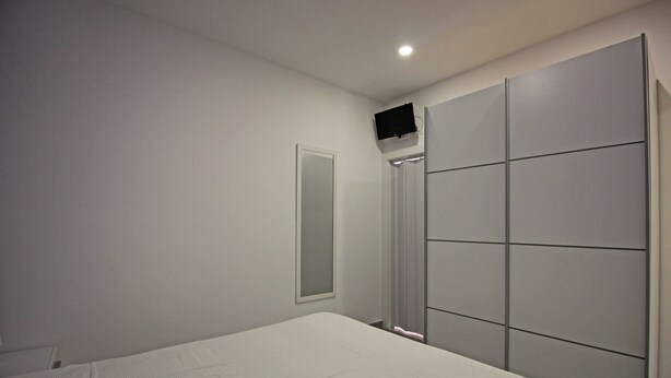 Quarto com cama, guarda-roupa, espelho e televisão na parede.