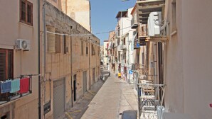 Uma rua estreita em área urbana, com edifícios em ambos os lados, um carro estacionado e fios de eletricidade suspensos.