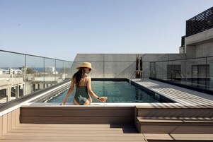 Mulher sentada à beira de uma piscina no terraço, com vista para a cidade.