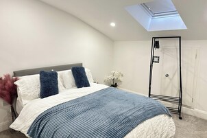 Quarto com cama, claraboia, porta branca e uma pequena planta.