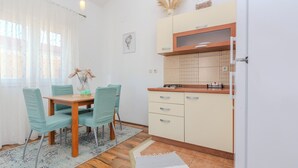 Cozinha compacta com área de refeições, apresentando uma mesa de madeira, cadeiras verde-água e painel de azulejos.