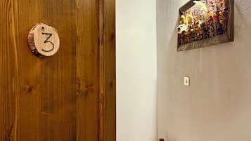 Uma porta de madeira com uma placa de número, uma cama com colcha floral e um objeto decorativo na parede.