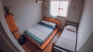 Quarto compacto com uma cama de solteiro, uma pequena janela e ar-condicionado fixado na parede.