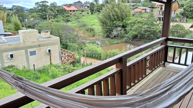 Um deck de madeira com uma rede, vista para uma área residencial com casas e vegetação.