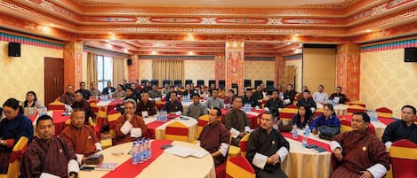 Sala de conferência com mesas redondas, participantes e um candelabro.
