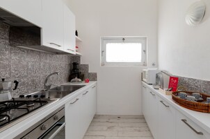 Uma cozinha compacta com armários brancos, fogão a gás, pia e janela.