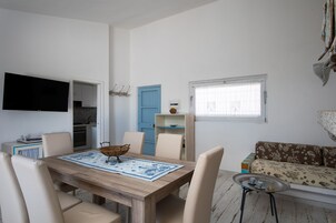Uma área de refeições com uma mesa de madeira, cadeiras bege e um jogo de mesa azul estampado.