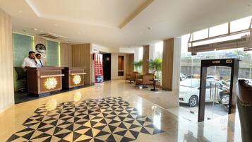 Um hall de hotel com piso estampado geométrico, balcões de recepção, uma grande janela e vista para carros estacionados lá fora.