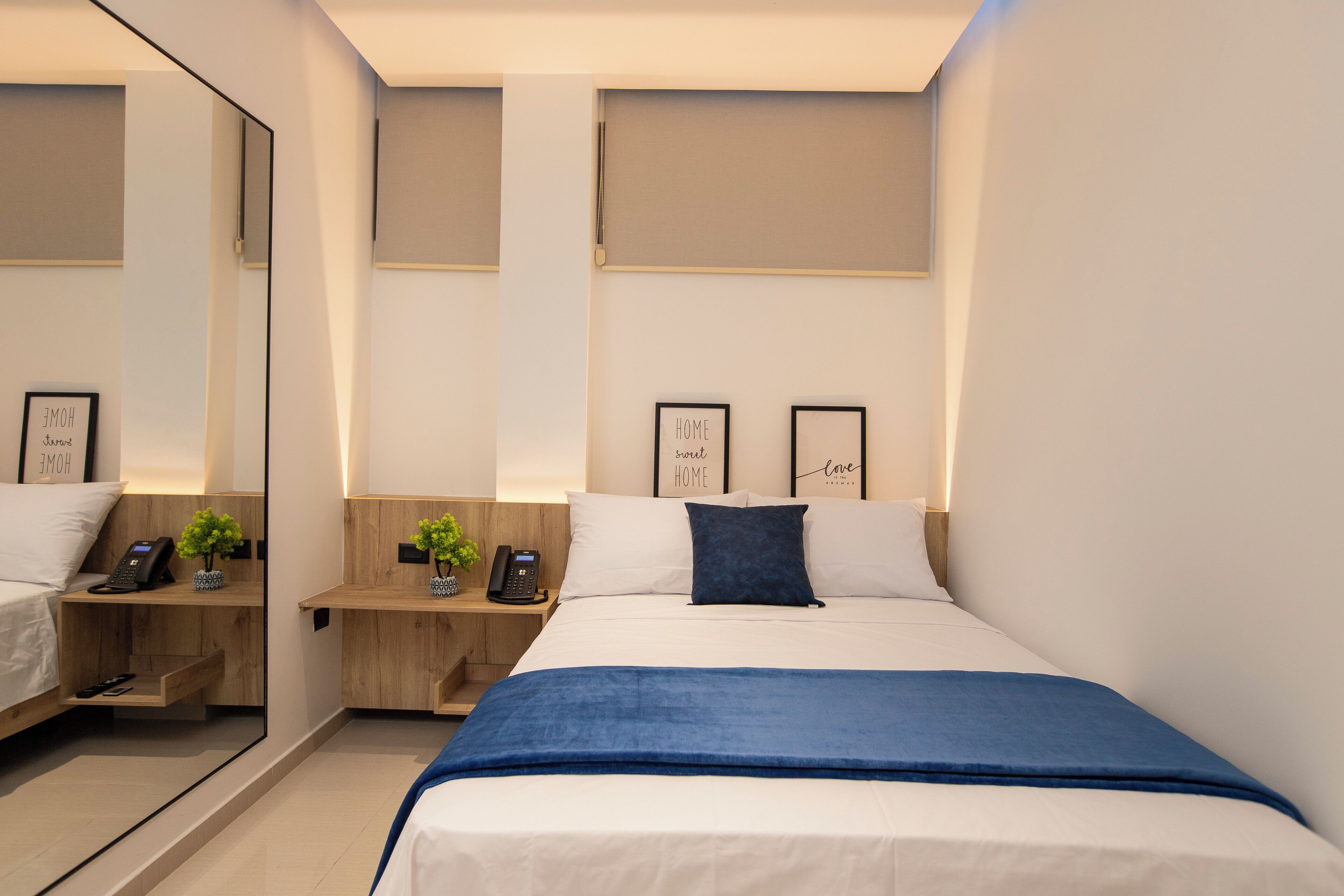 Quarto de hotel moderno com uma cama grande, mesas de cabeceira, espelho e quadros na parede.