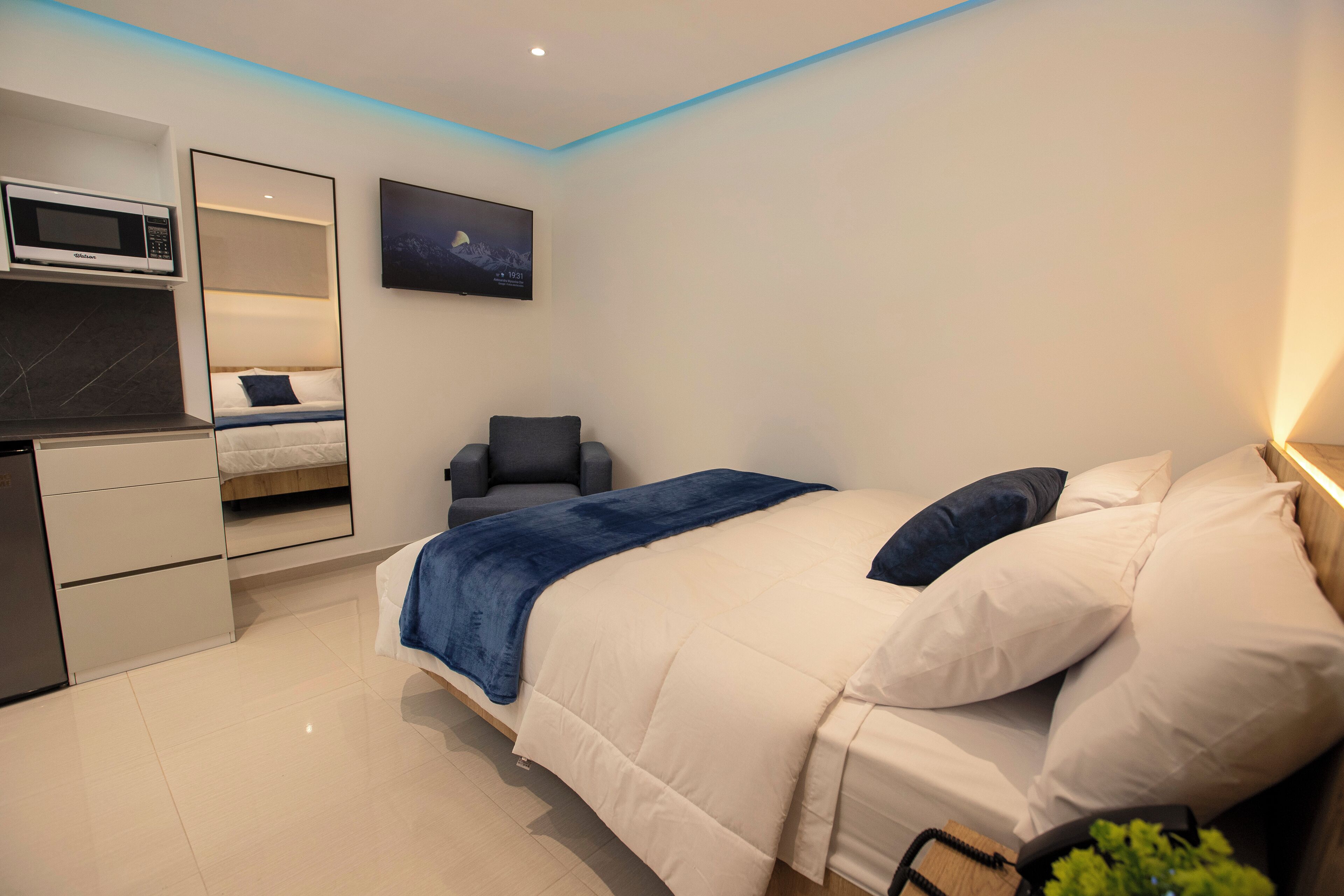 Quarto moderno com cama, cadeira, micro-ondas e televisão.