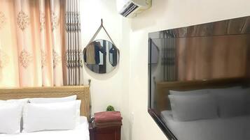 Quarto de hotel com uma cama, mesa de cabeceira, espelho e uma grande tela de televisão.