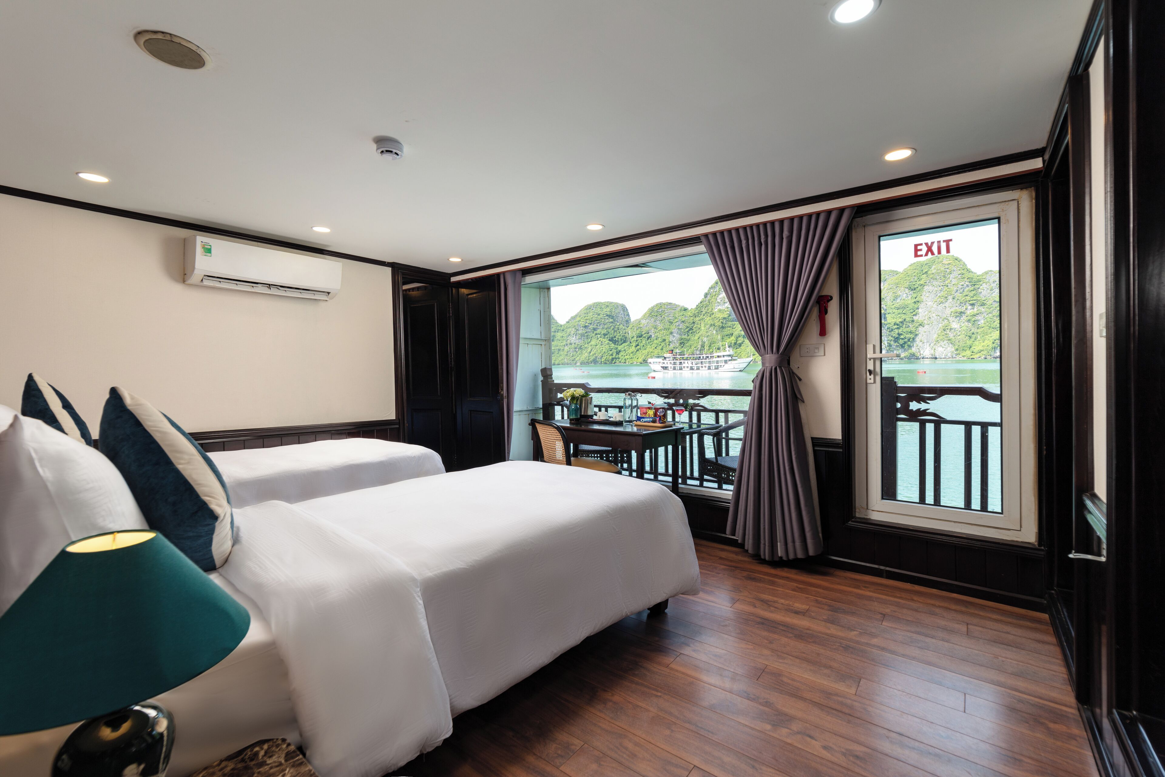 Quarto de hotel com duas camas, uma mesa e vista para um barco na água.