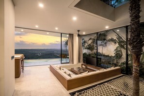 Quarto moderno com uma cama grande, uma televisão e vista para um pôr do sol sobre a água.