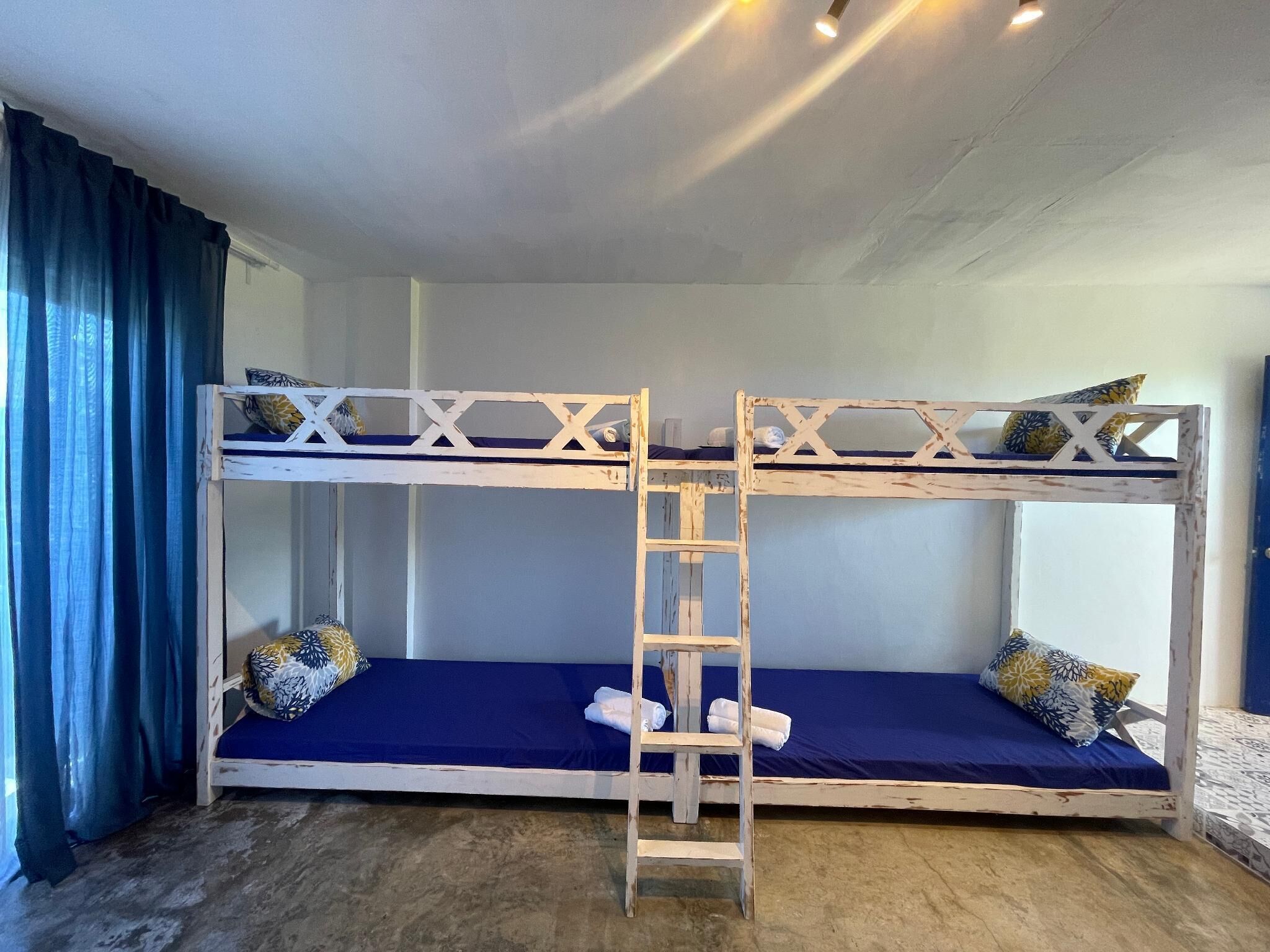 Quarto com beliches, escada de madeira, roupa de cama azul e almofadas estampadas.
