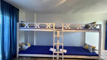Quarto com beliches, escada de madeira, roupa de cama azul e almofadas estampadas.
