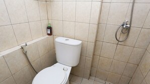Um banheiro pequeno com azulejos, vaso sanitário, chuveiro e um frasco de álcool em gel na parede.