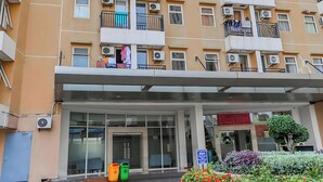 Um edifício residencial com vários andares, varandas, aparelhos de ar condicionado e uma entrada com portão.