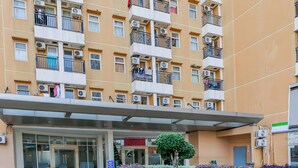 Um edifício residencial de vários andares com varandas, aparelhos de ar condicionado e entrada com portão.