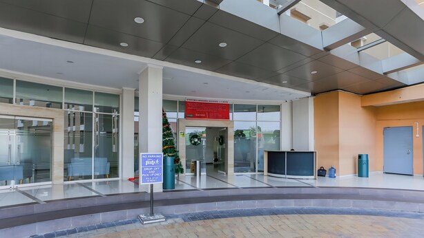 Entrada de um edifício moderno com portas de vidro, uma placa indicando que não há estacionamento e um pinheiro de Natal.