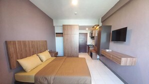 Quarto de hotel moderno com uma cama grande, televisão fixada na parede e uma pequena área de cozinha.
