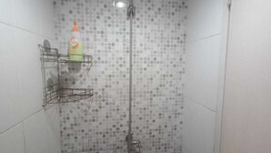 Um chuveiro pequeno, com azulejos, um chuveiro manual e um dosador de sabonete numa prateleira.