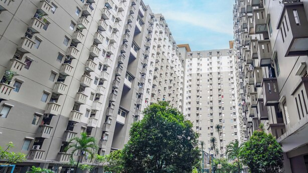 Um edifício residencial alto com várias varandas, céu claro e vegetação ao primeiro plano.