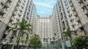 Um edifício residencial alto com várias varandas, um parquinho e áreas verdes ao redor.