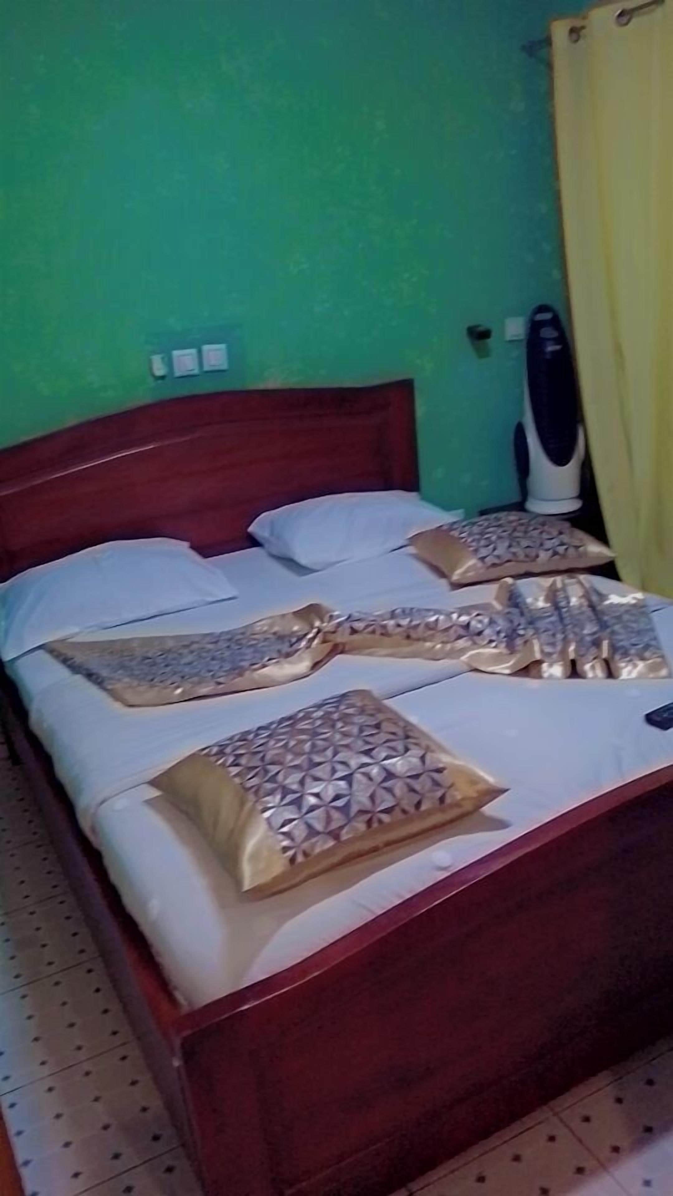 Cama com almofadas estampadas, mesa de cabeceira com abajur e parede verde.