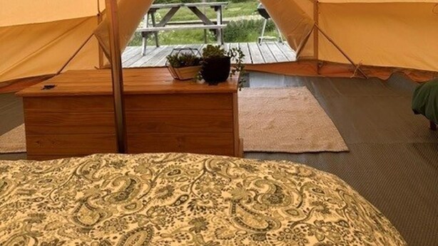Uma tenda com plataforma de madeira e uma cama com colcha estampada.