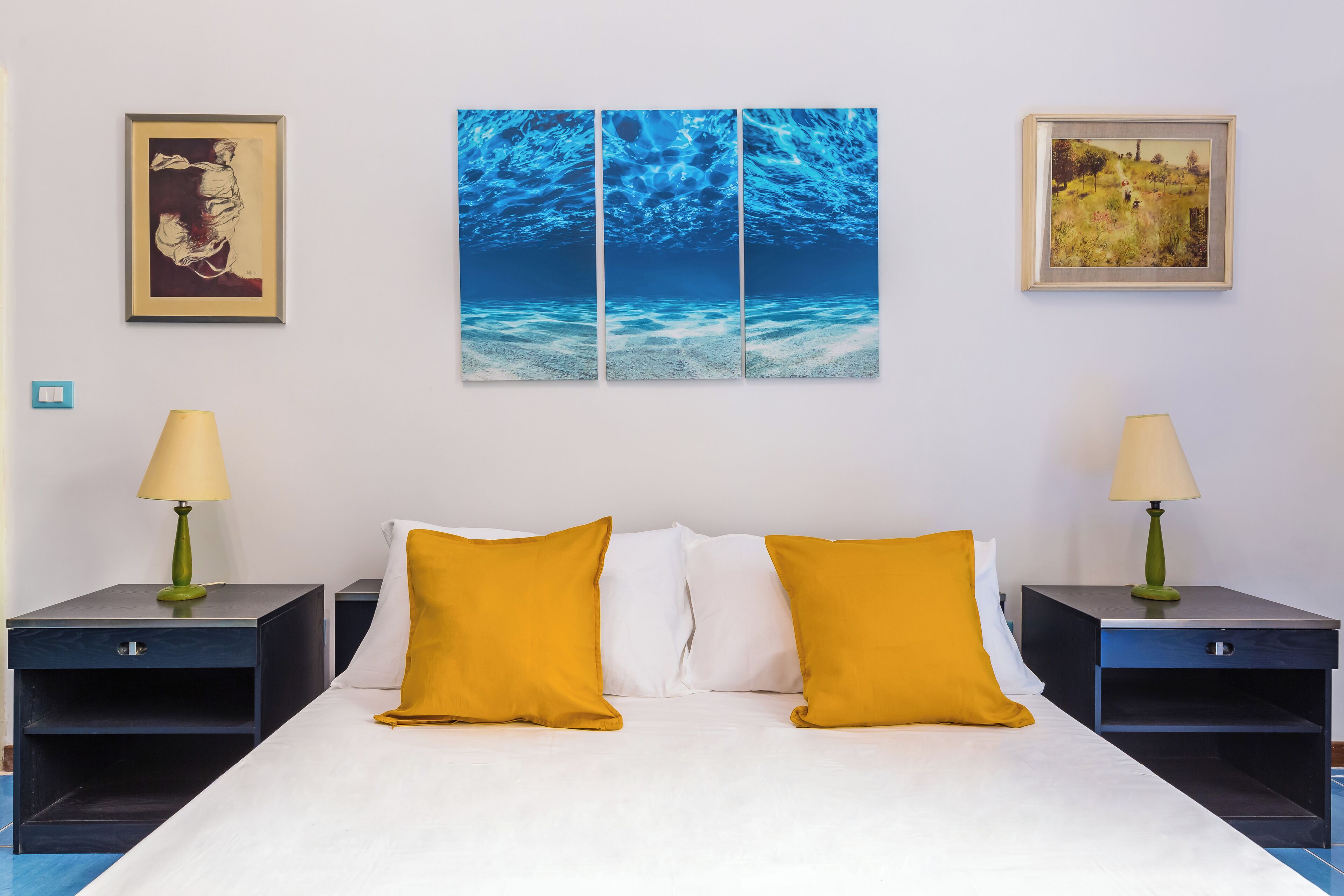 Quarto de hotel com uma cama, duas mesas de cabeceira, duas luminárias e três quadros na parede.