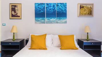 Quarto de hotel com uma cama, duas mesas de cabeceira, duas luminárias e três quadros na parede.
