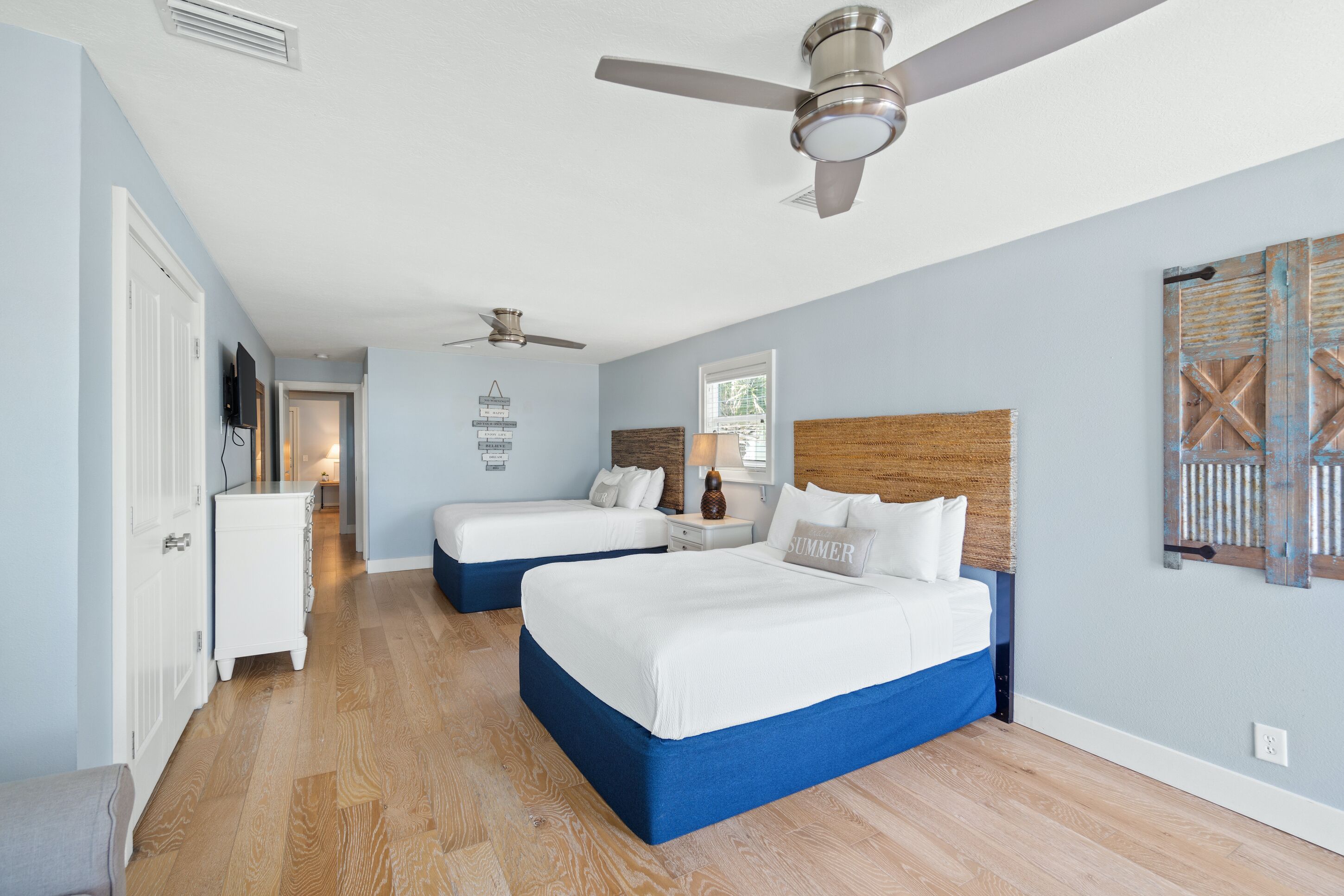 Quarto com duas camas, um ventilador de teto, uma cabeceira de madeira e uma janela.