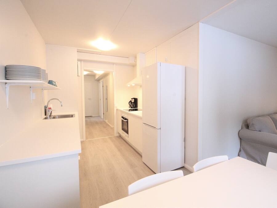 Cozinha moderna com eletrodomésticos brancos, sala de jantar com mesa e cadeiras, e um sofá na sala de estar.