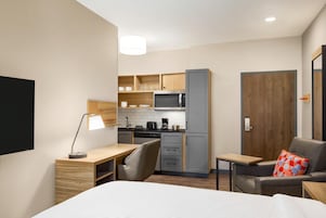 Quarto de hotel compacto com cozinha compacta, cama, escrivaninha e área de estar.