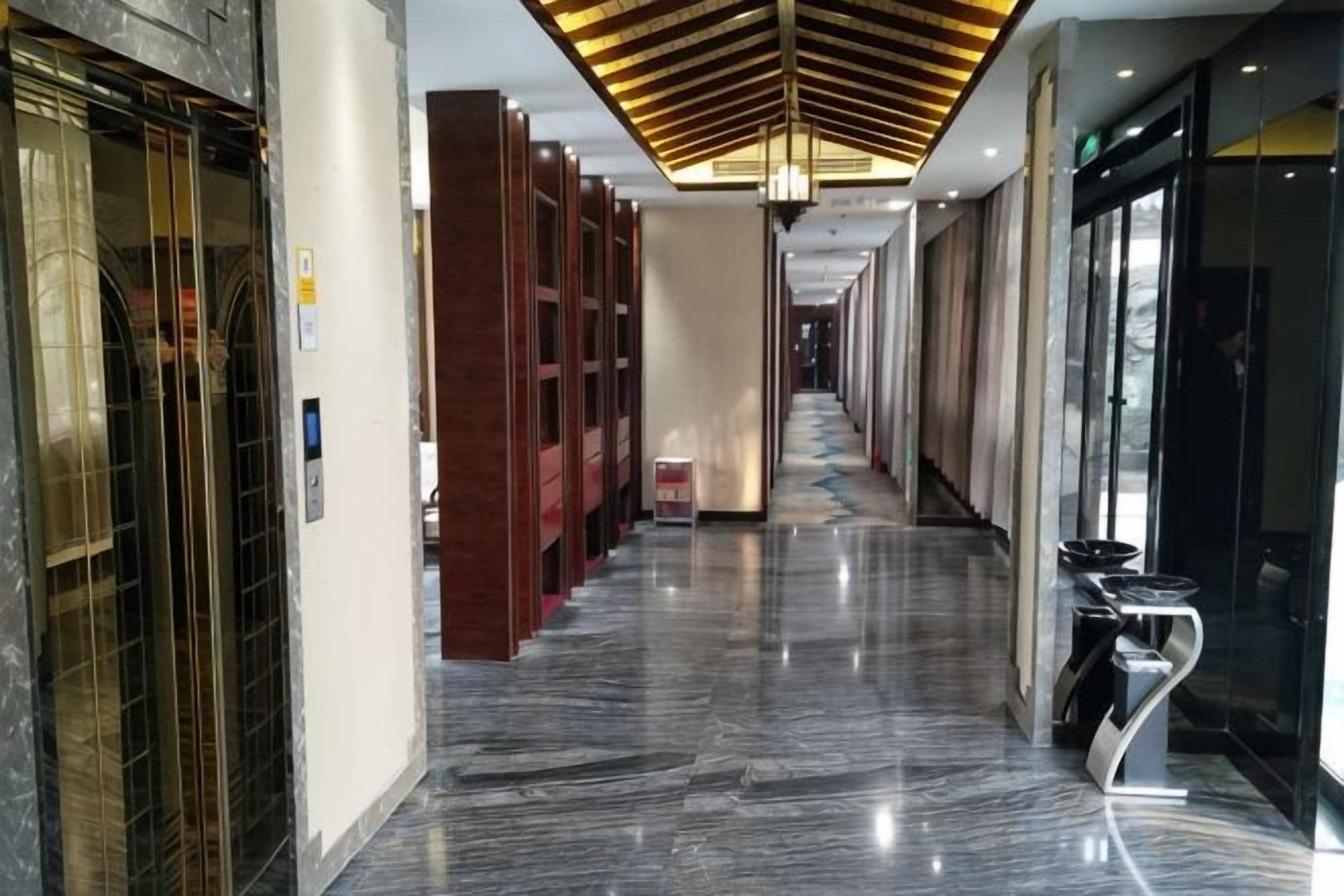 Um corredor com piso de mármore, estantes de madeira e um elevador moderno.