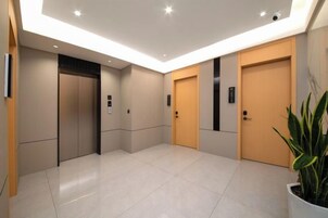 Interior moderno com dois elevadores, uma planta em vaso e uma porta.