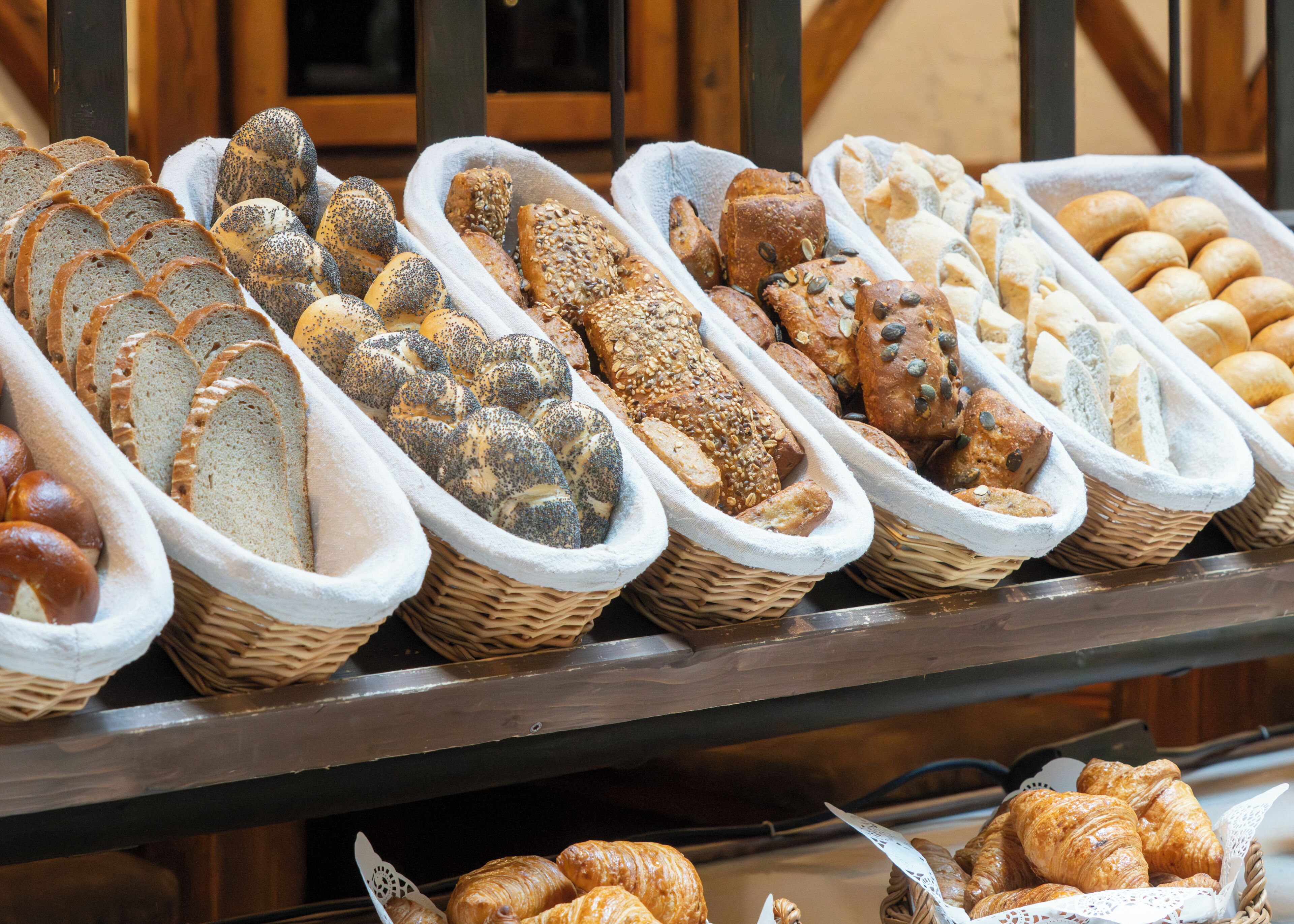 Diversos pães e doces expostos em cestas sobre uma prateleira.