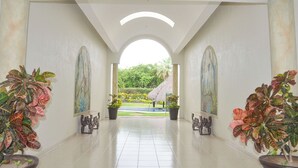 Um corredor com vista para um jardim tropical, plantas em vasos e uma estrutura com telhado de palha.