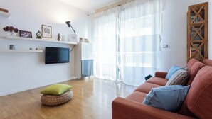 Uma sala de estar moderna com uma TV de tela plana, um sofá com almofadas, um banquinho de vime e um armário de madeira com porta de vidro.