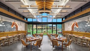 Restaurante moderno com pé-direito alto, vigas de madeira e grandes janelas que oferecem vista para o exterior.
