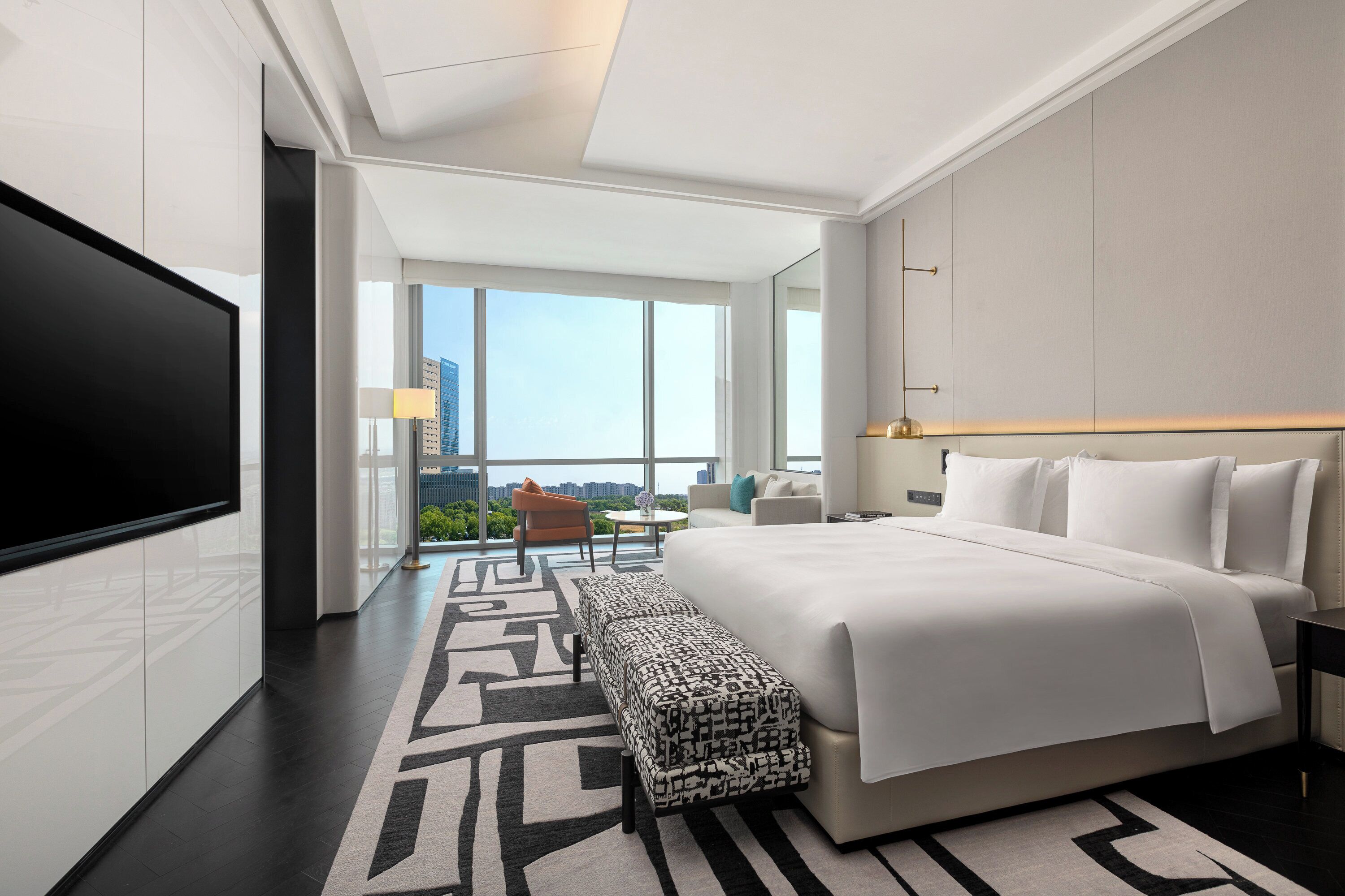 Quarto de hotel moderno com uma cama grande, televisão de tela plana, área de estar com vista e uma janela ampla.