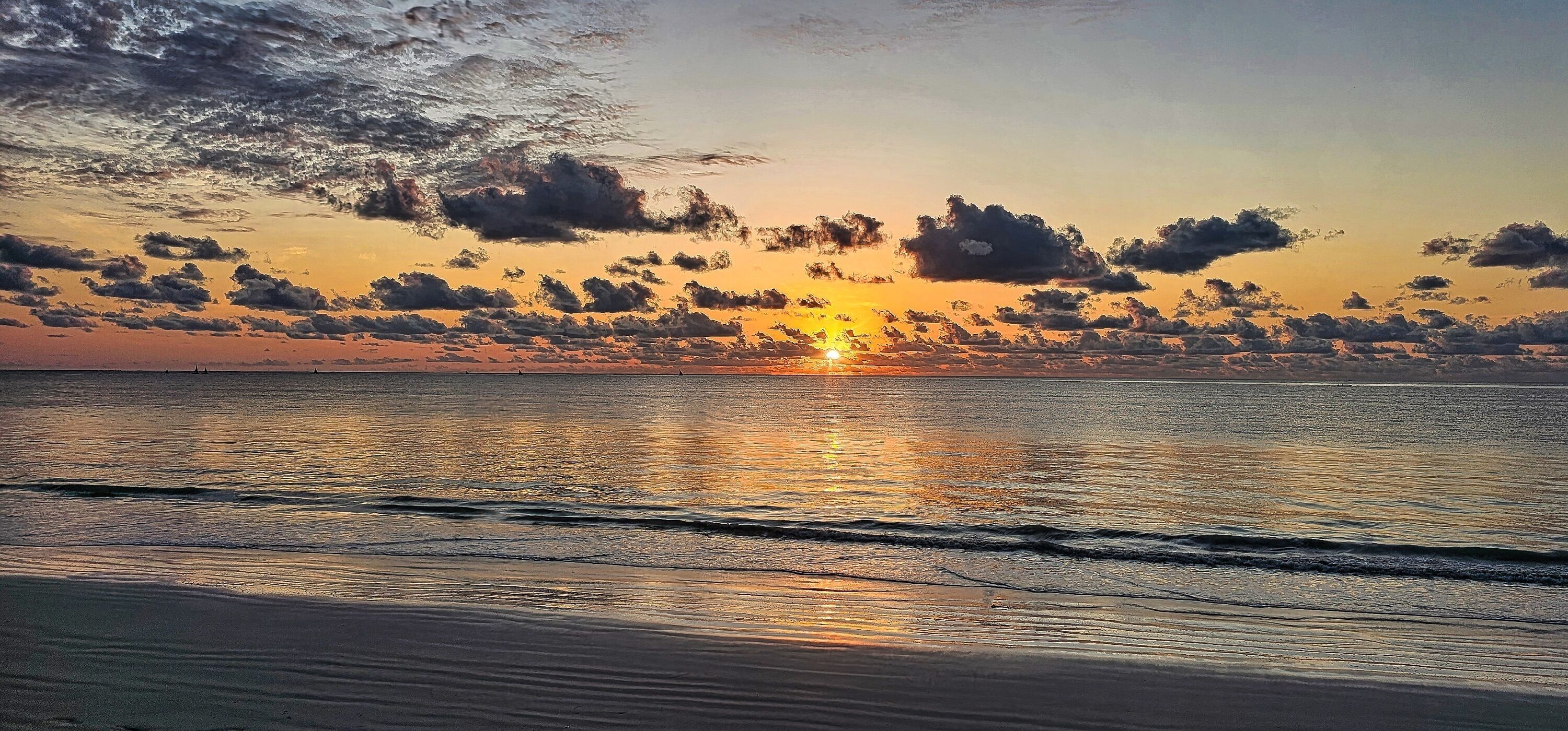 Um pôr do sol sobre um mar calmo, com céu claro e nuvens.
