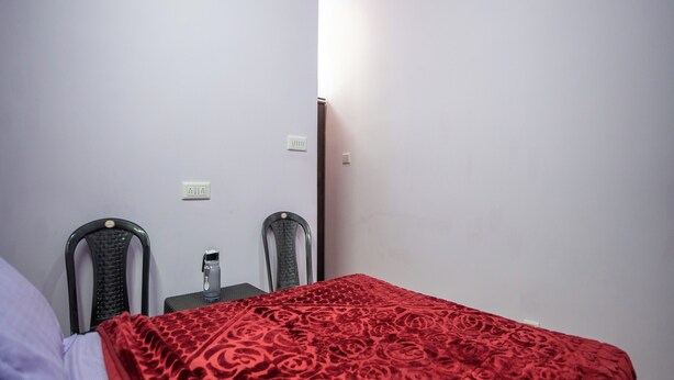 Um quarto pequeno e pouco mobiliado, com uma cama de solteiro, duas cadeiras e uma mesa.