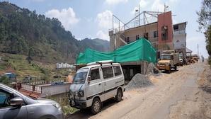 Um canteiro de obras com uma van branca estacionada em uma estrada de terra, cercado por materiais de construção e um edifício em construção.