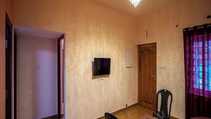 Um quarto amplo com piso de madeira, um candelabro, uma televisão e uma porta.