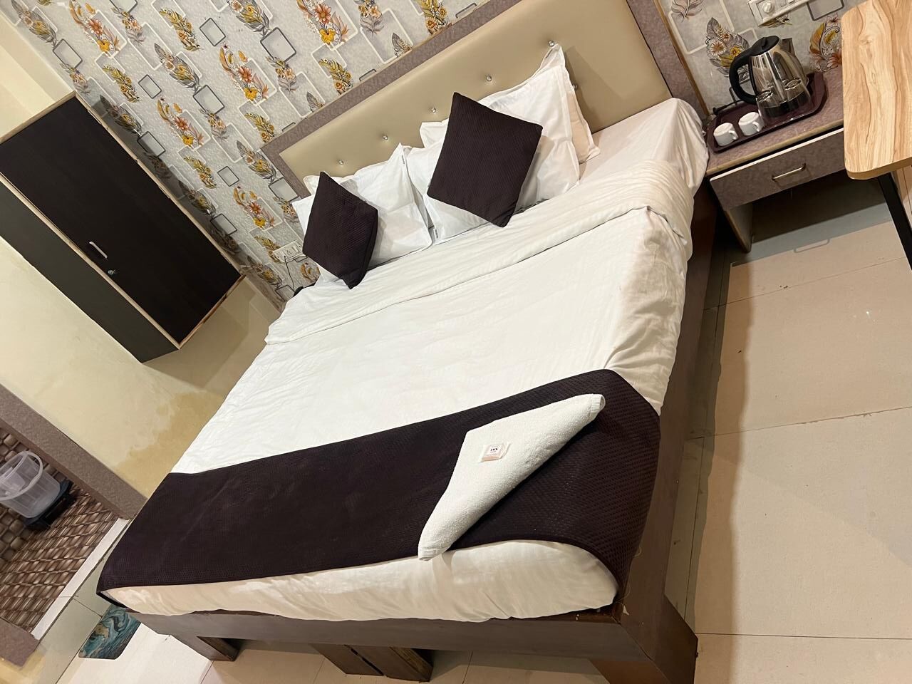 Cama bem arrumada com colcha branca e preta, duas almofadas e uma toalha dobrada.