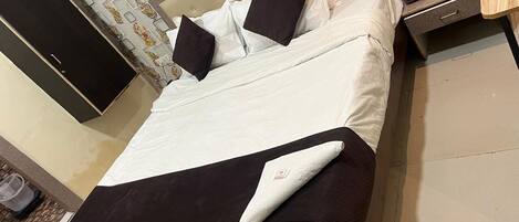 Cama bem arrumada com colcha branca e preta, duas almofadas e uma toalha dobrada.