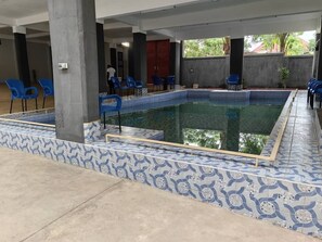 Piscina com azulejos estampados em azul e branco, rodeada por cadeiras azuis e um deck de concreto.