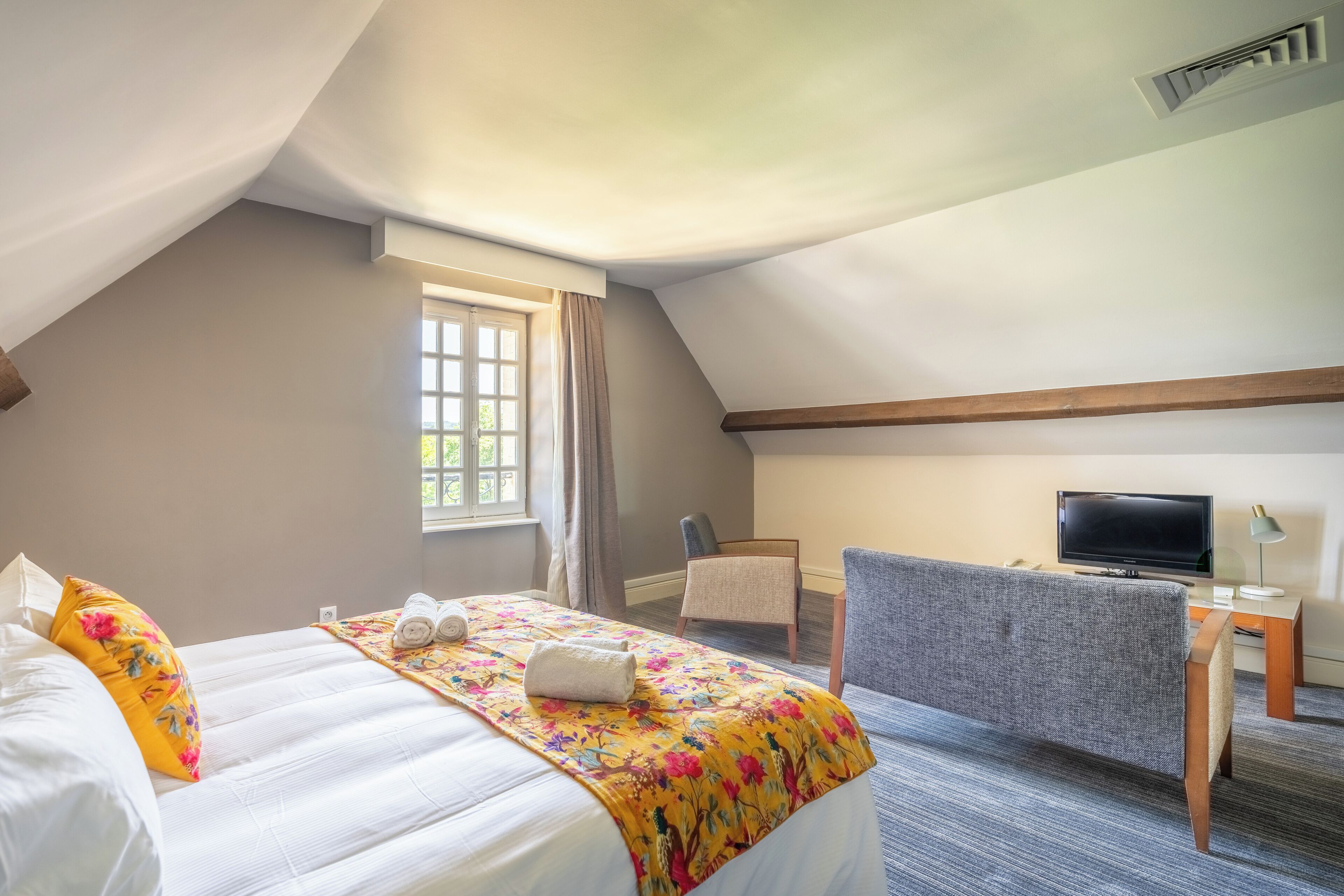 Quarto de hotel com cama, escrivaninha com televisão e janela.