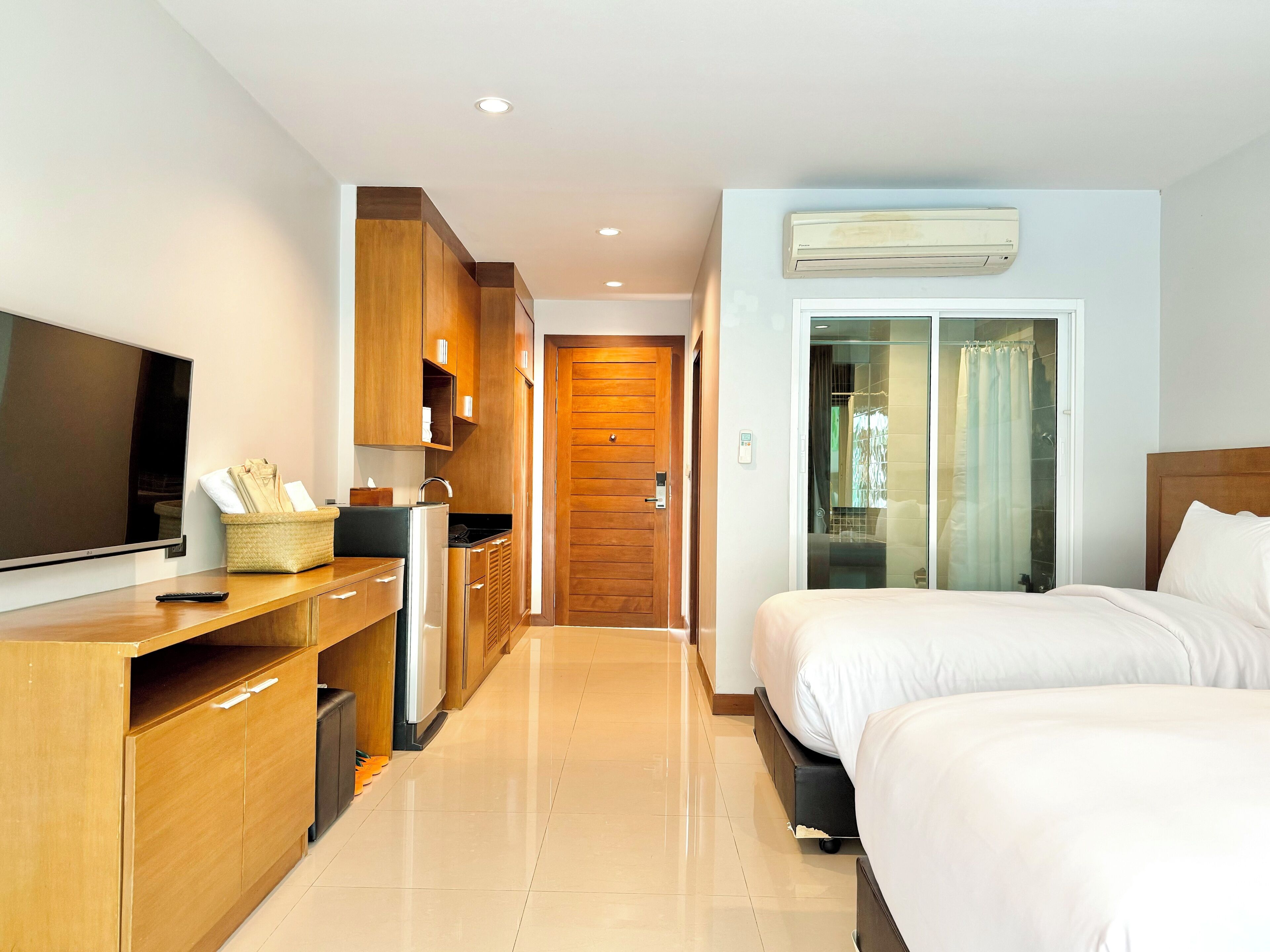 Quarto de hotel com cama, televisão, cozinha compacta e área de chuveiro.